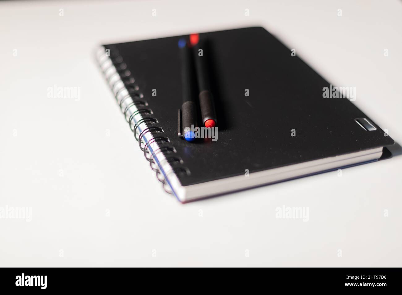Closed black spiral binding notebook with pens isolated on white ...