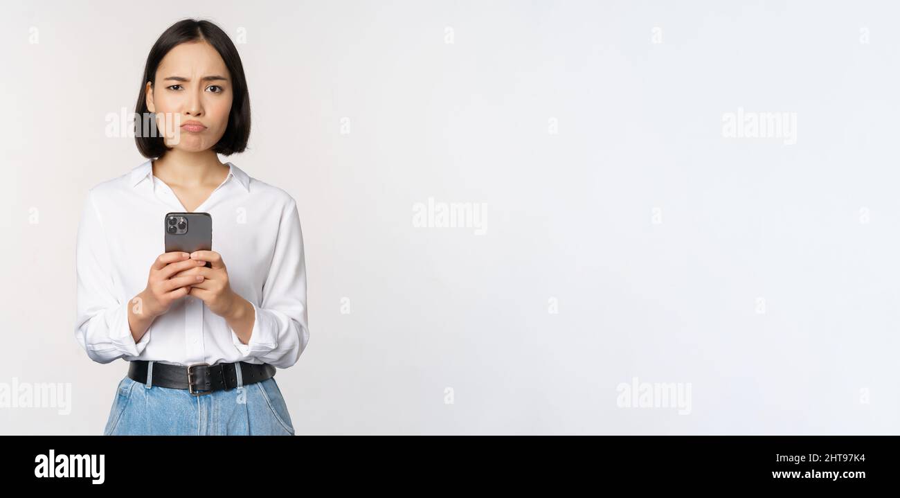 Asian woman holding smartphone and looking with doubt, disappointed ...