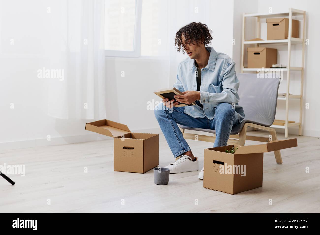 handsome guy sitting on a chair unpacking with box in hand moving ...