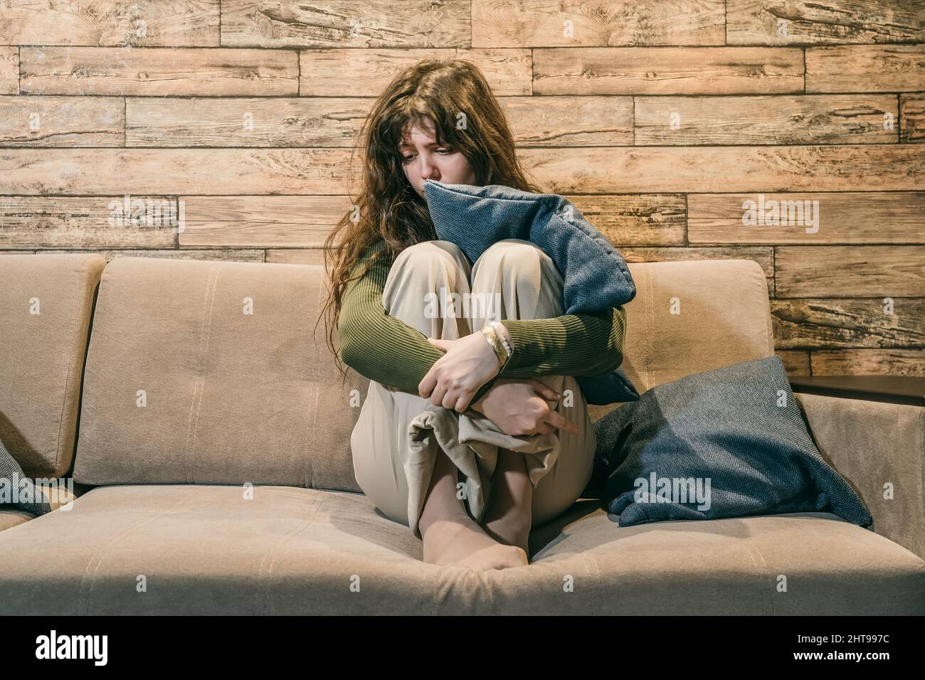 Sad girl sitting on couch hugging her legs with hands. Depression ...