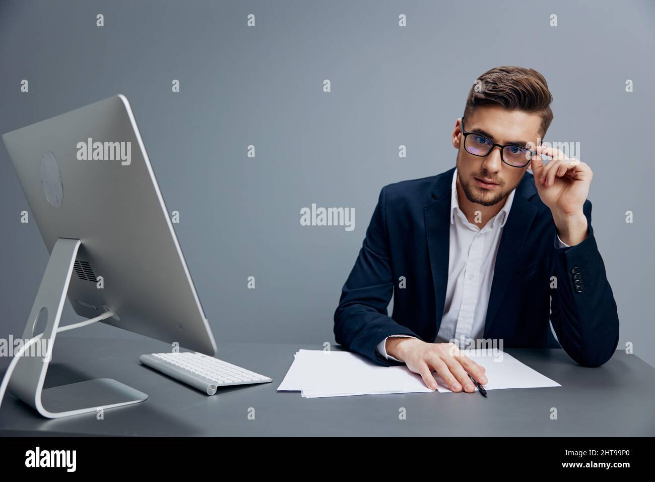 a man in a suit sitting at a desk in front of a computer Gray ...