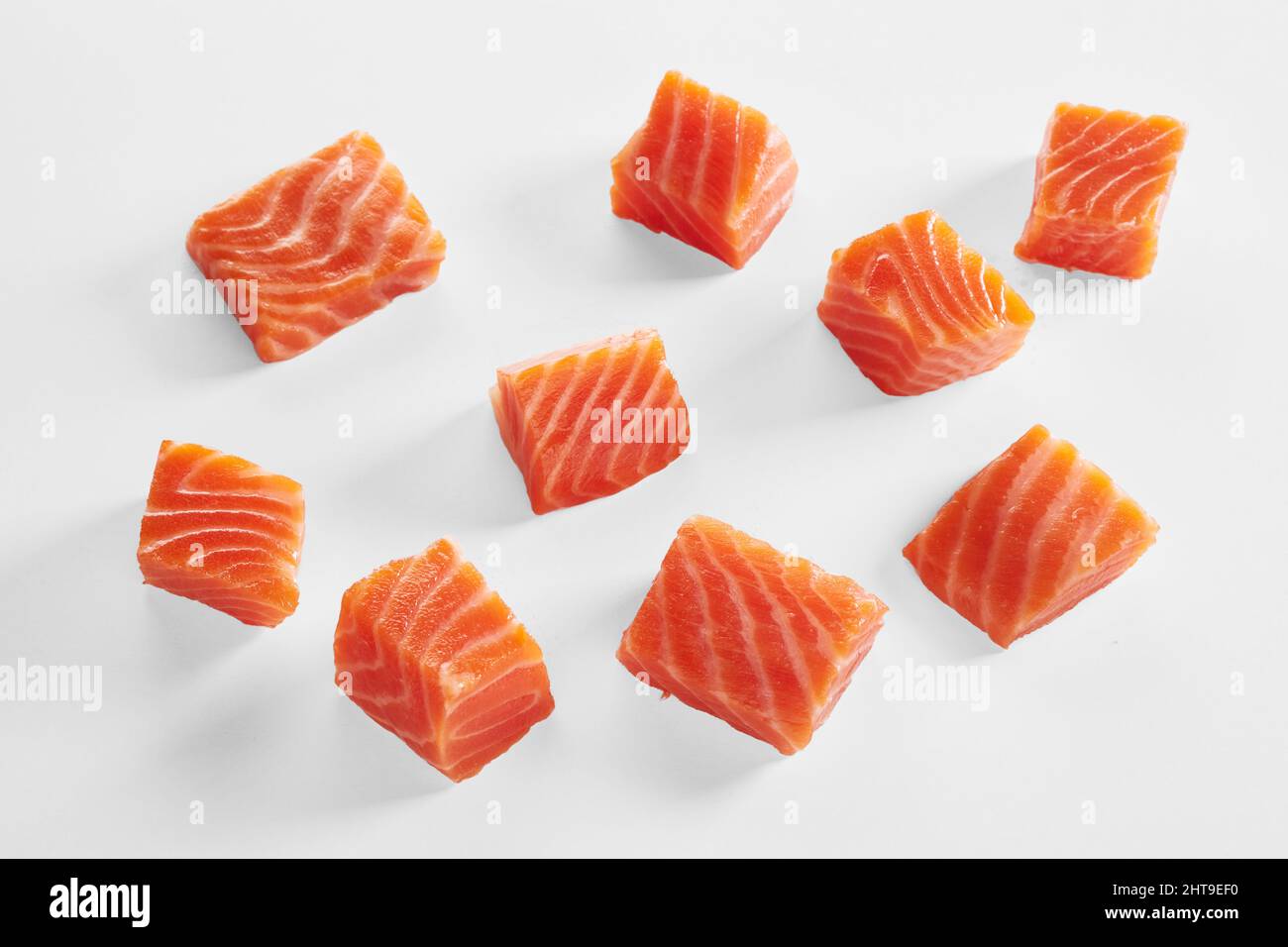 Uncooked salmon fillet cut in cube-shaped slices arranged on a white ...