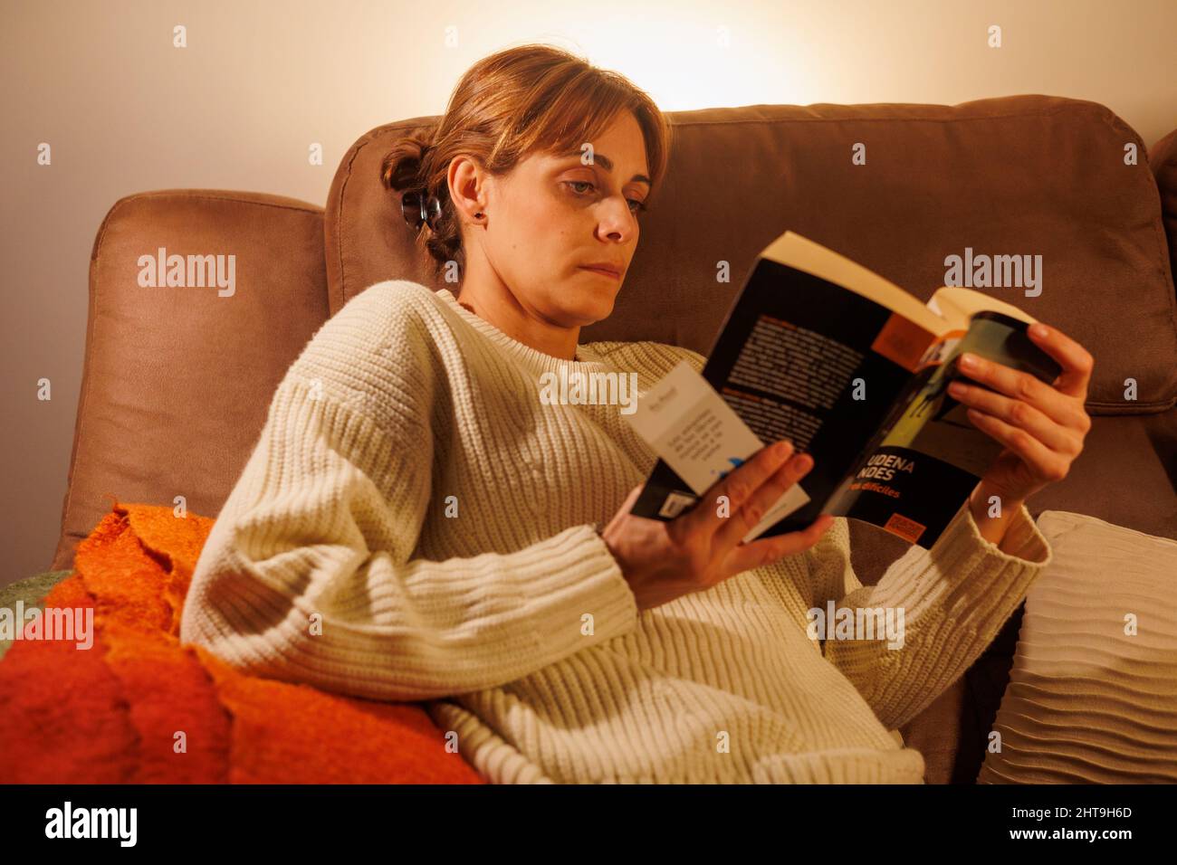 Female reading a book sitting on the couch at home Stock Photo - Alamy