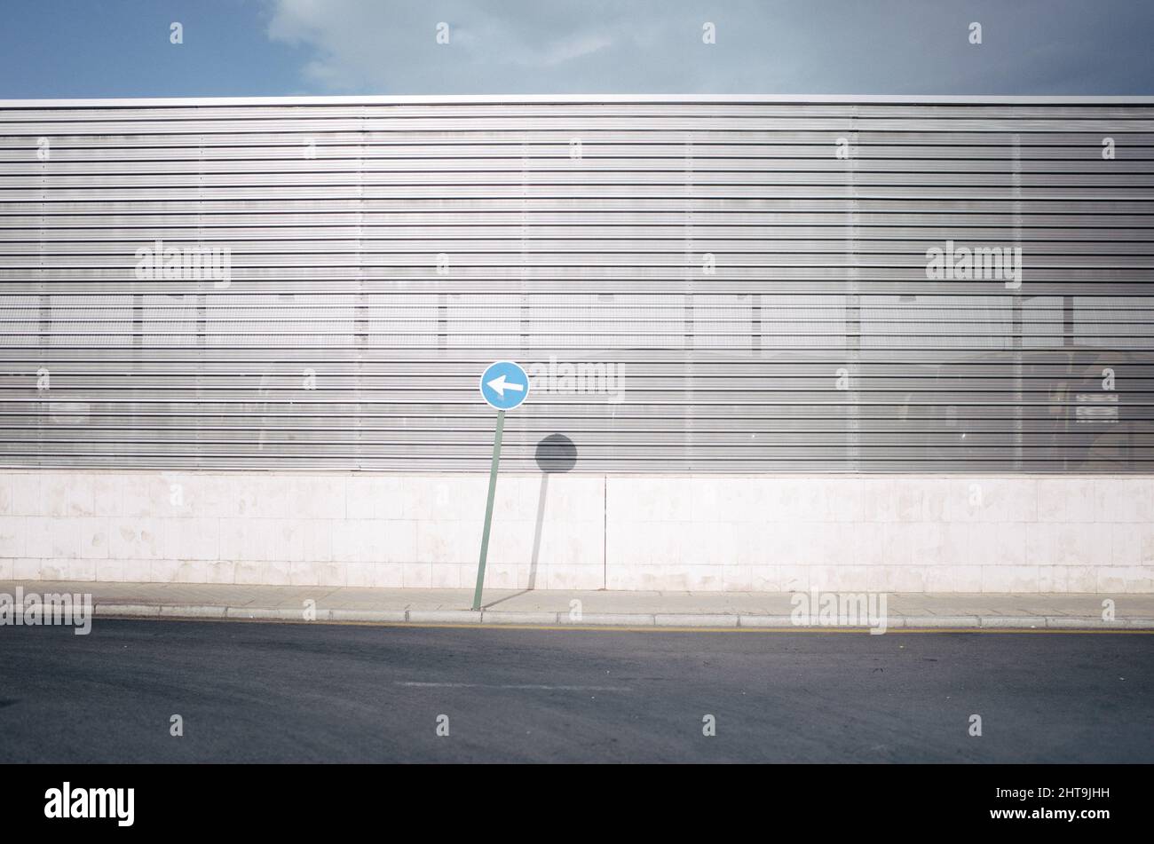 Photo of an arrow road sign in front of wall of commercial building ...