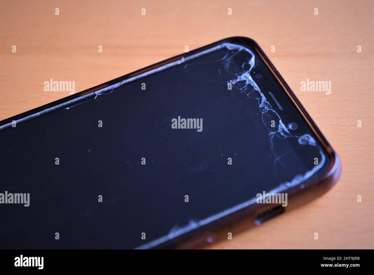 Black smartphone with cracked screen protector, isolated on a brown ...