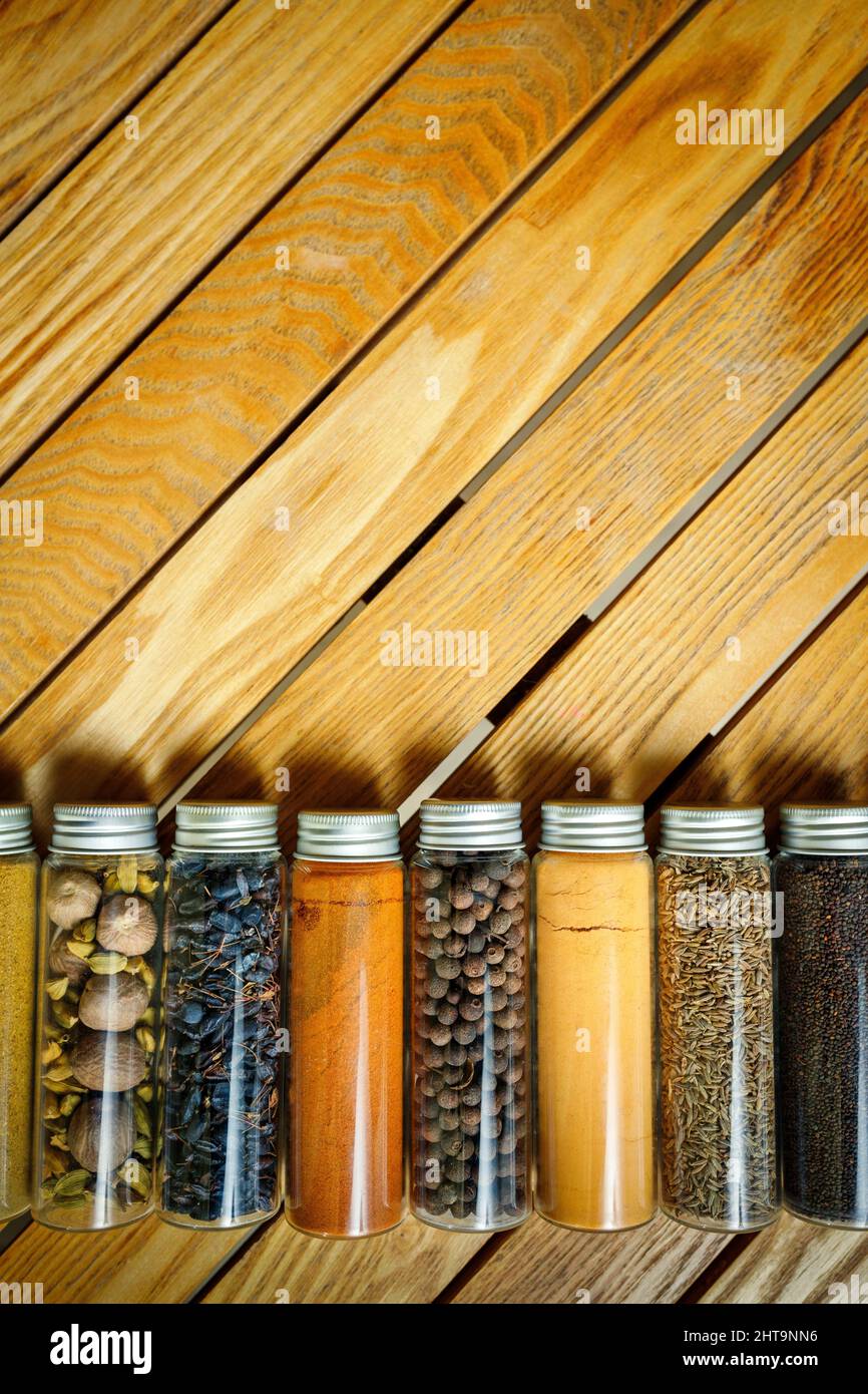 Different multi-colored spices in jars lie on a board background with ...