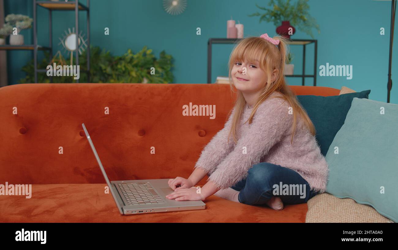 Little school kid girl use laptop computer sitting on sofa alone at ...