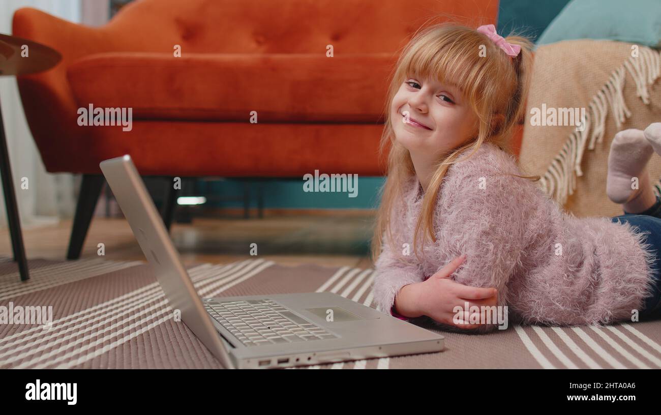 Little school kid girl use laptop computer lying on floor alone at home ...