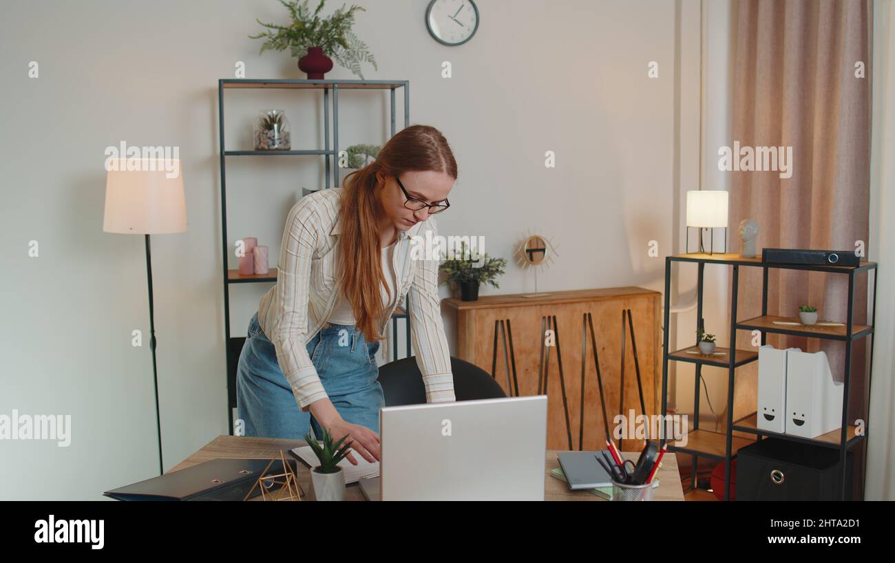 Young professional Caucasian woman in shirt, standing by desk in home ...