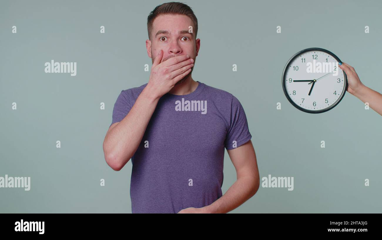 Confused man with anxiety checking time on clock, running late to work ...