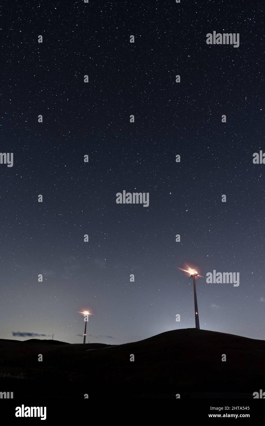 Vertical shot of a night with a starry sky next to an electric windmill ...