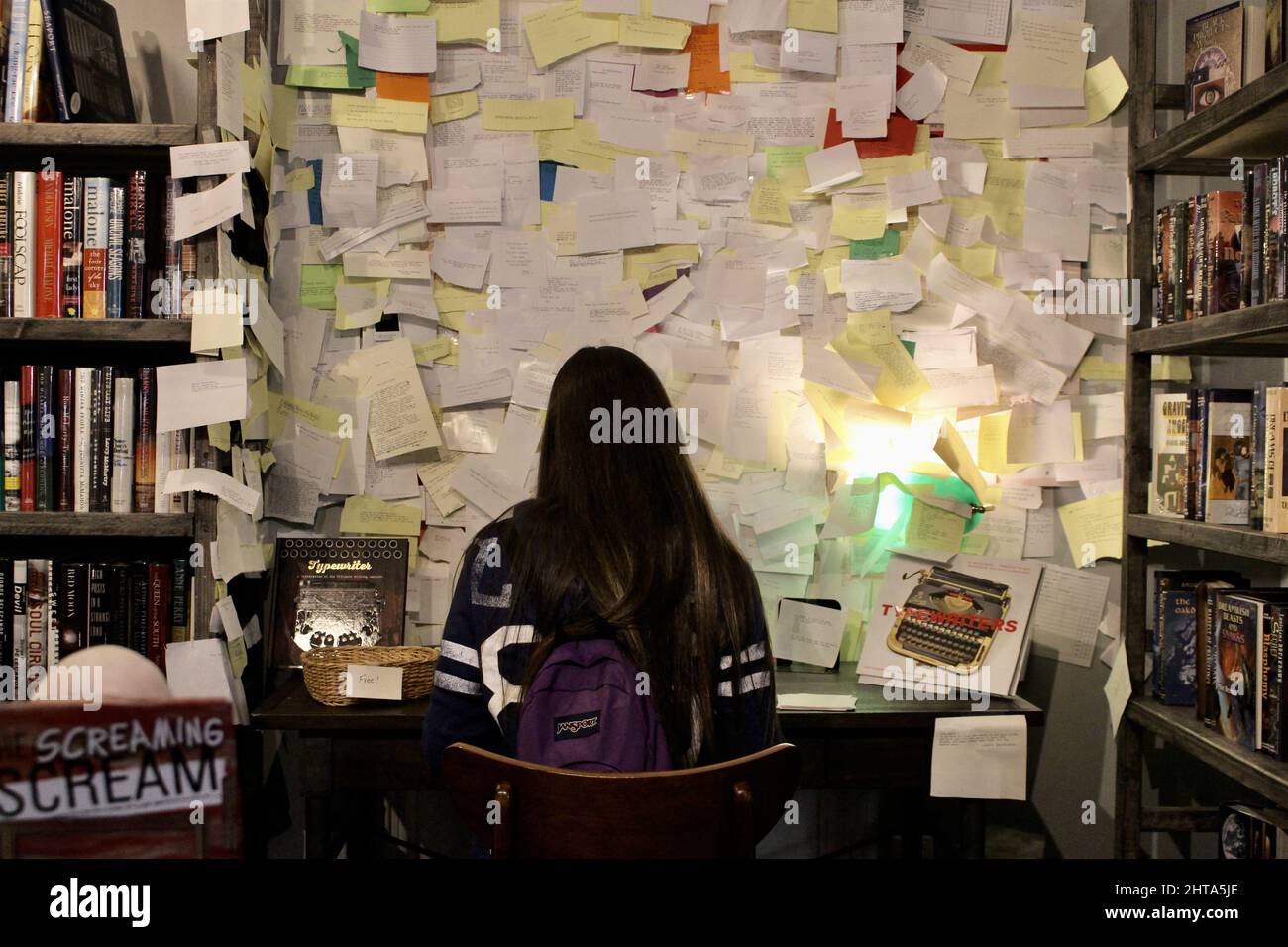 Rear view of a girl using a typewriter in front of messages taped to ...