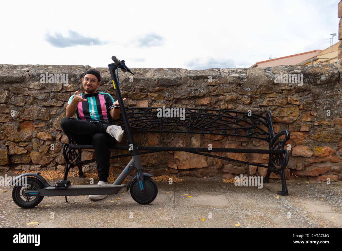 Man sitting on a bench showing his electric scooter near a horizontal ...