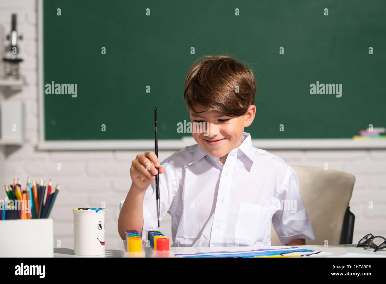 Portrait school kid boy doing art homework, holding pencil, writing ...