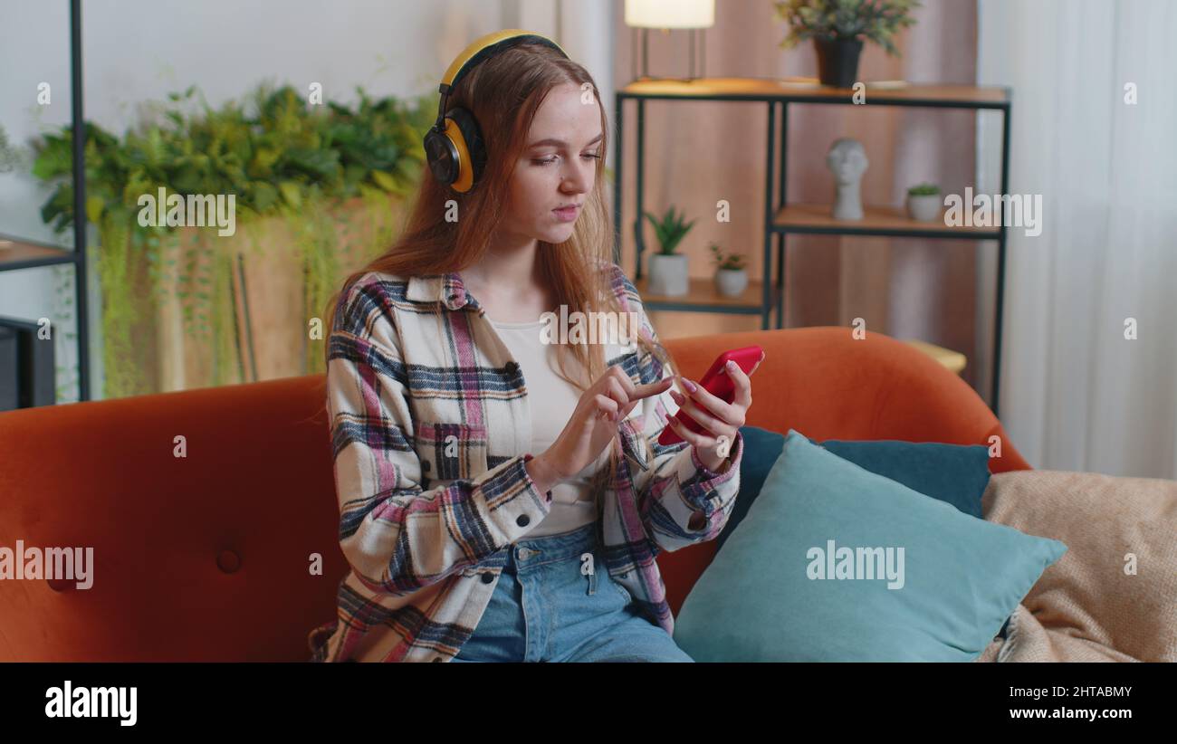 Overjoyed young woman in wireless headphones dancing, singing on cozy ...