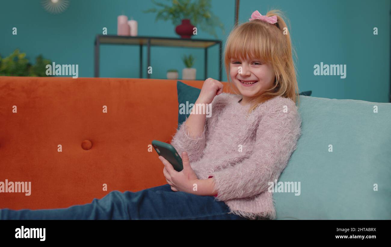 Happy little school kid girl use mobile cell phone doing winner gesture ...