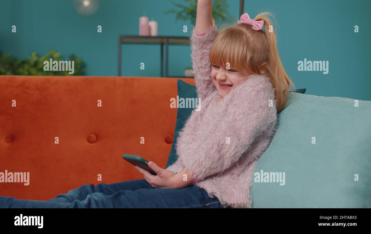 Happy little school kid girl use mobile cell phone doing winner gesture ...