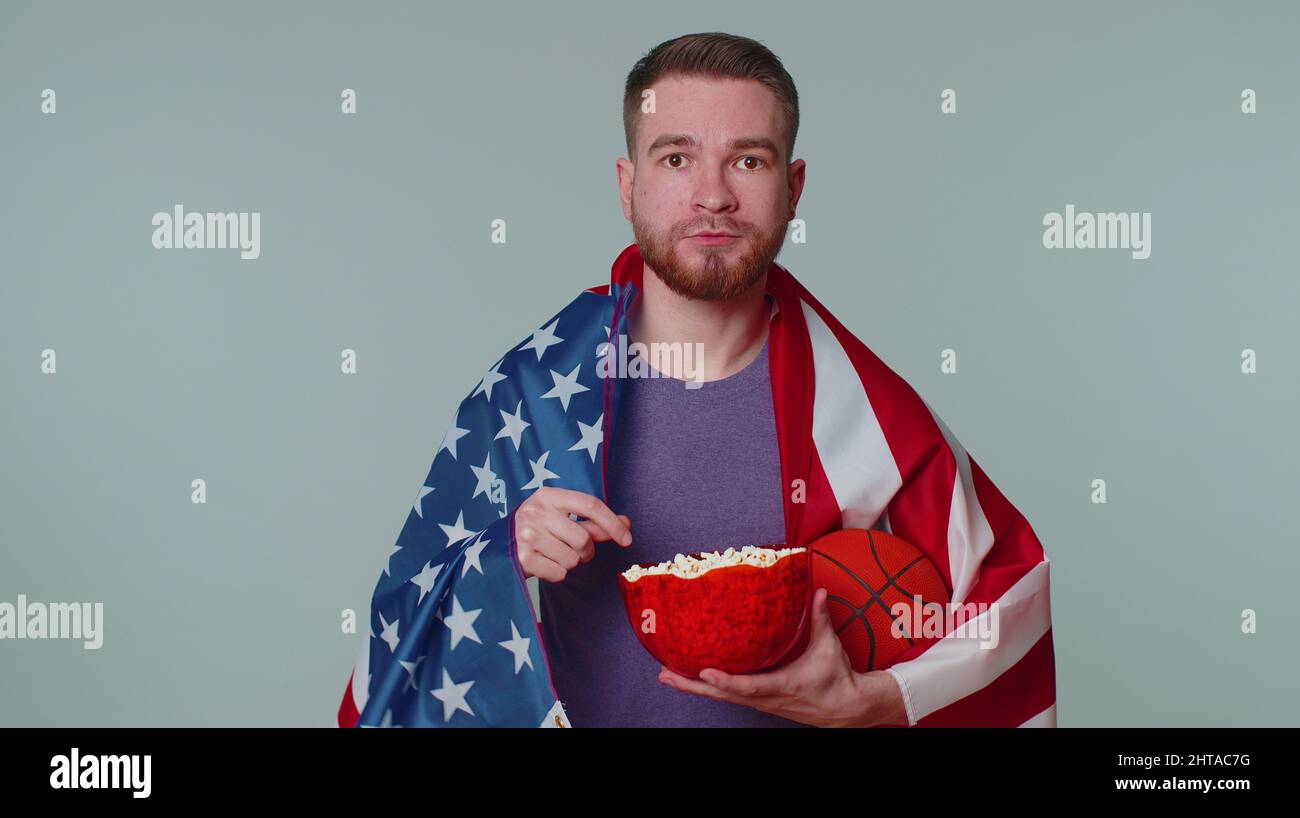 Bearded young man basketball fan eating popcorn doing winner gesture ...