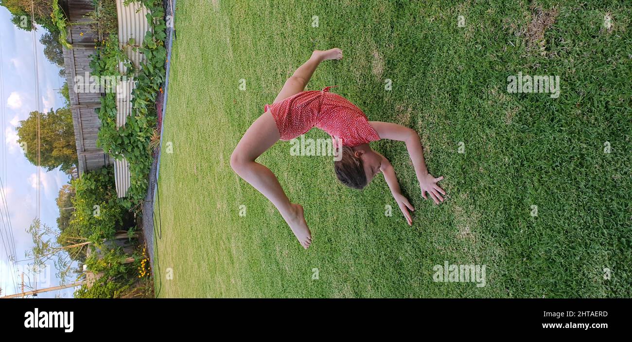 Vertical shot of a young girl doing gymnastics in her backyard ...