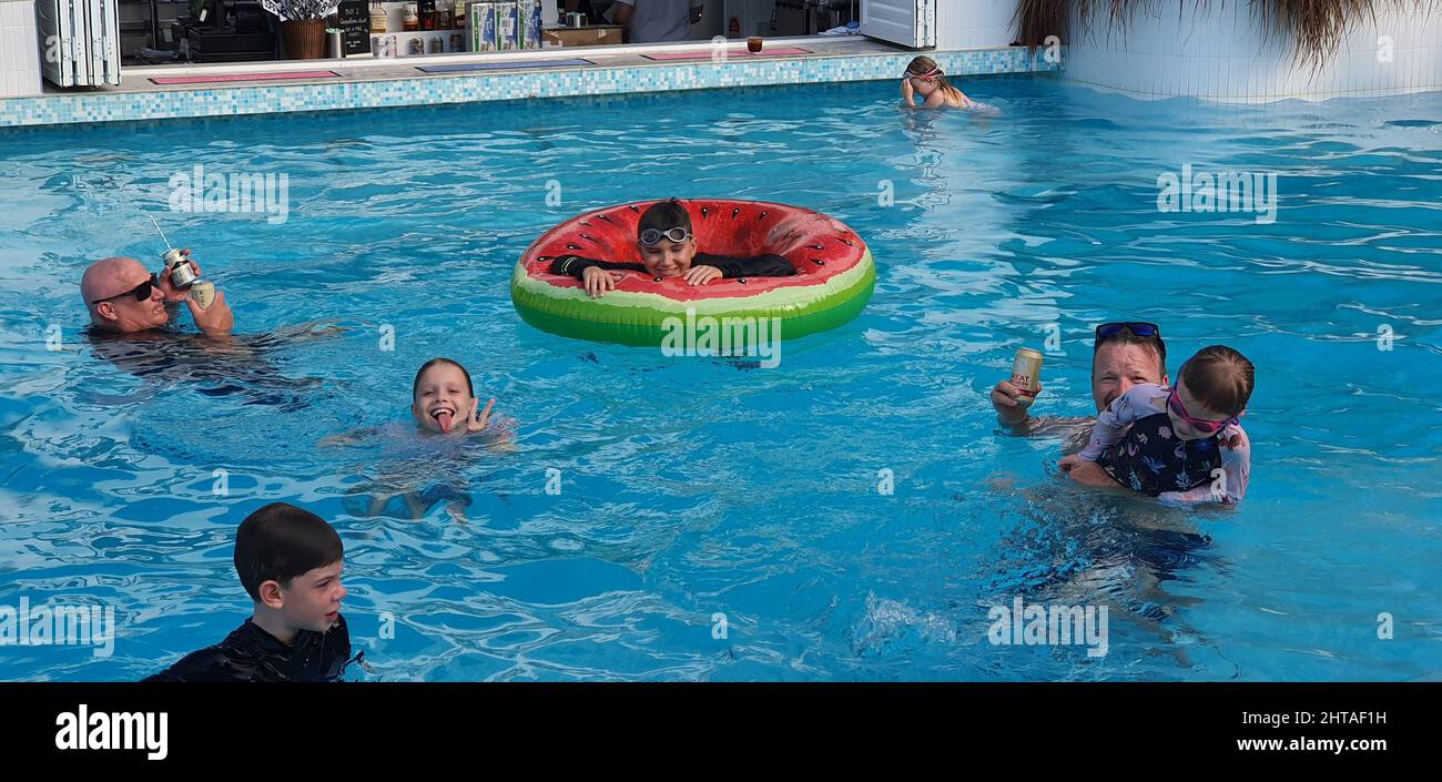 Bright summer day with a family enjoying swimming in a clear blue pool ...