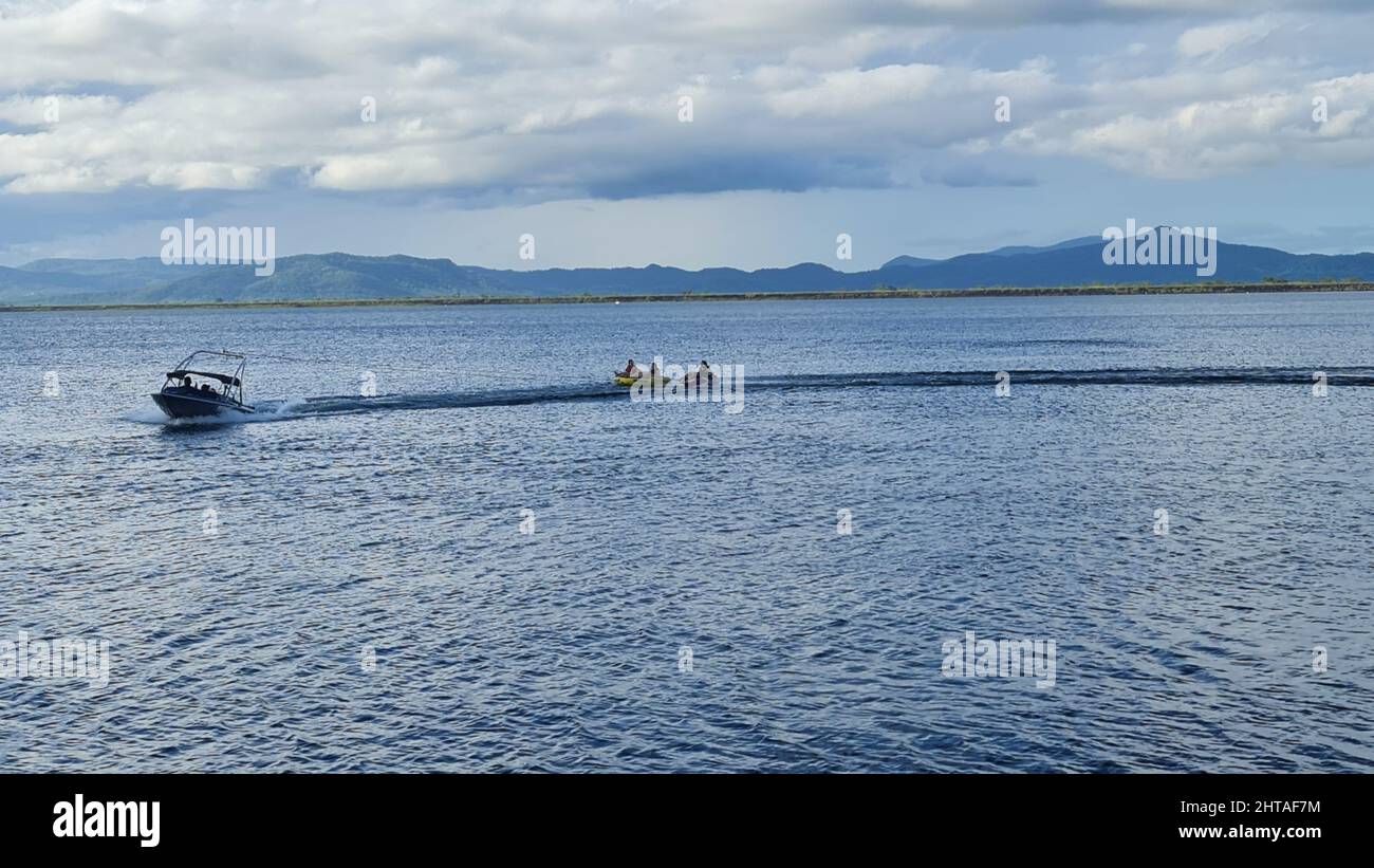Bright summer day at a beach with a family speed boating in the water ...