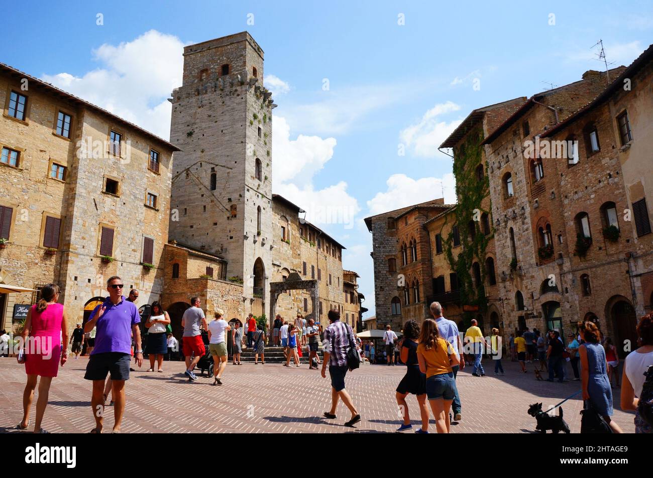 People walking in a square around old buildings and towers on a warm ...