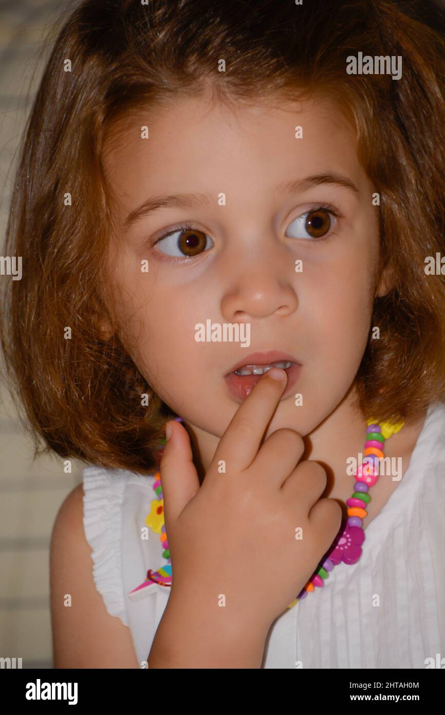 Portrait of a little girl with her finger on her lips with a thoughtful ...