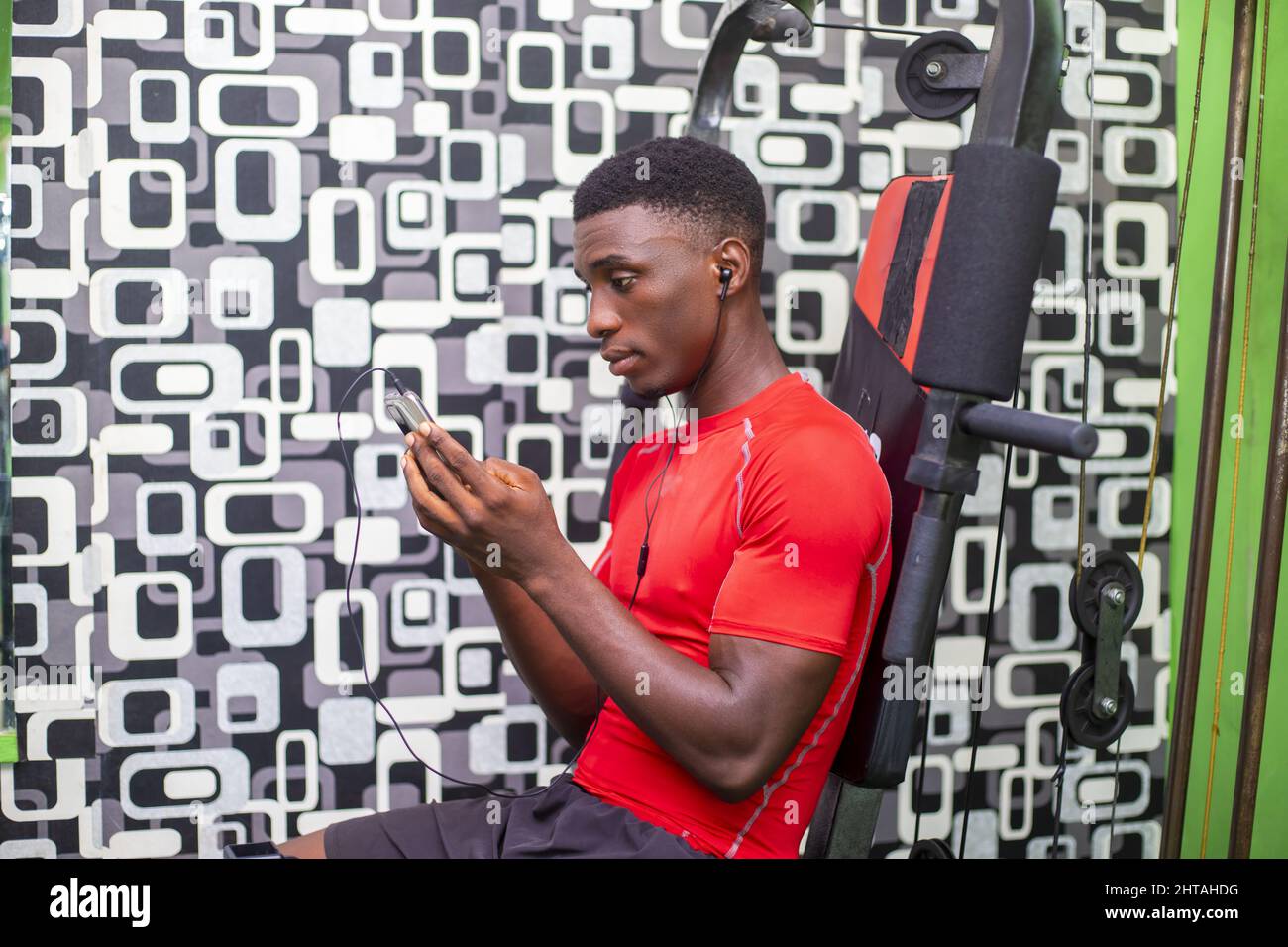 Young African guy using his phone while sitting on a pec deck machine ...