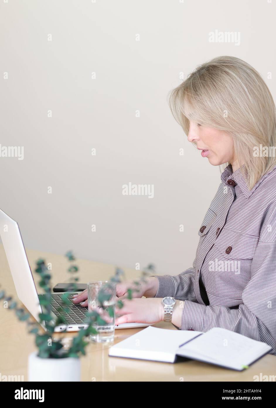 blond business woman working in an office, typing on a laptop ...