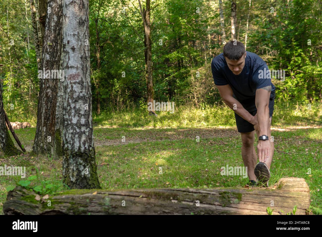 A young enduring athletic athlete is doing stretching in the forest ...