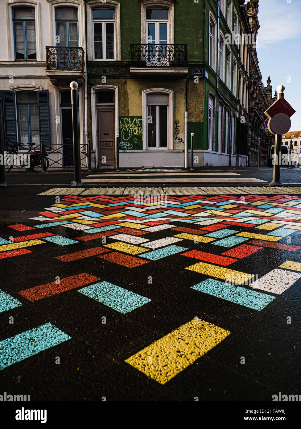 Vertical of wet asphalt with colorful patterns against an old green ...