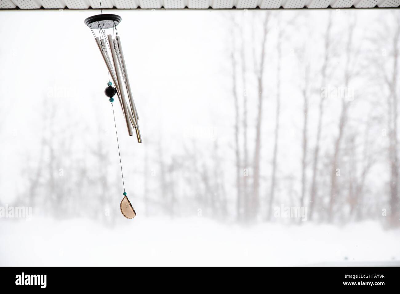 A wind chime with long metal tubes blowing in a winter snow storm Stock ...