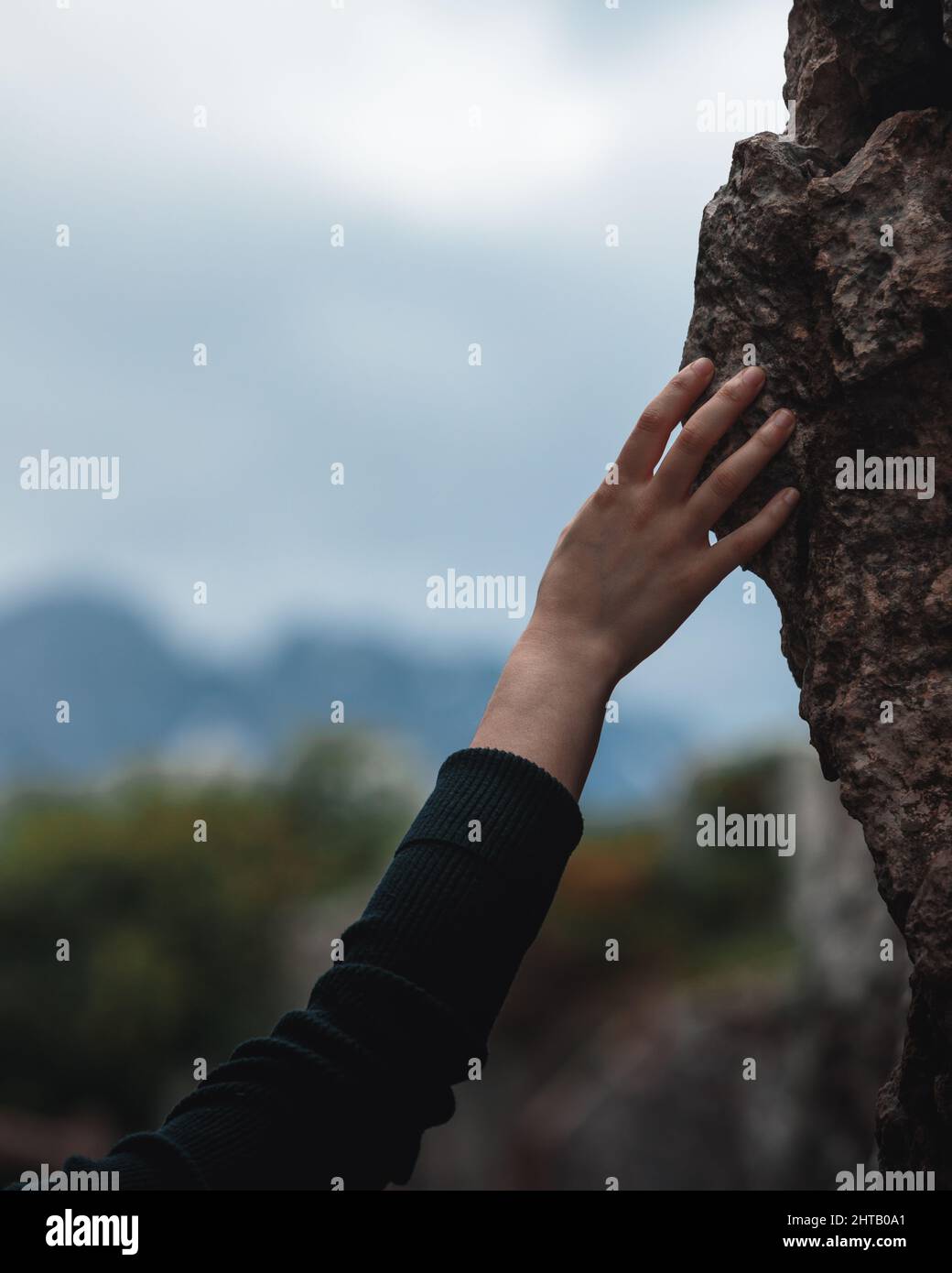 Vertical of a hand touching a piece of rock on a blurry background of ...