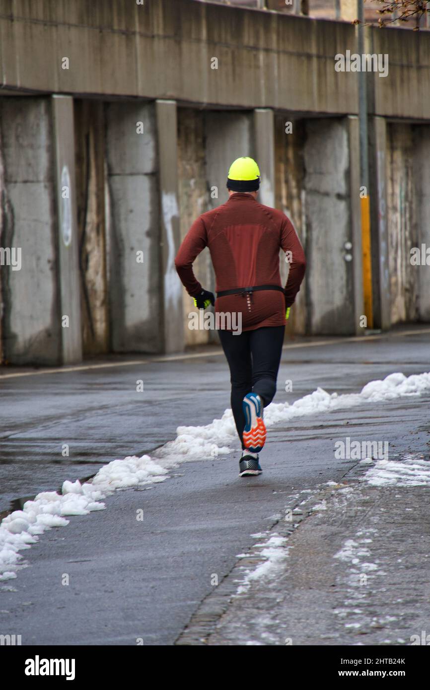Vertical shot of a back view of a sporty male running in the street ...