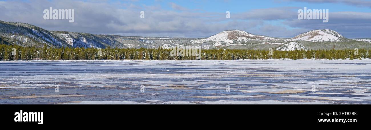 Panoramic scene of a snowy river, trees, blue sky and snowy mountains ...