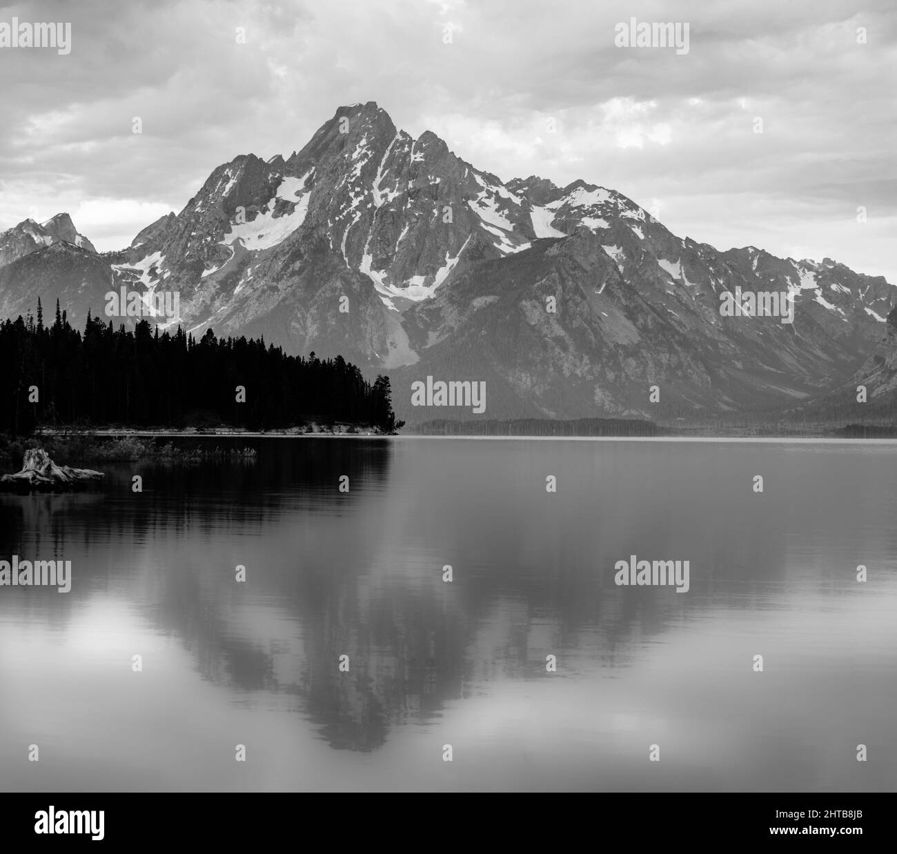 Grayscale shot of a lake with the reflection of dense forest and snow ...