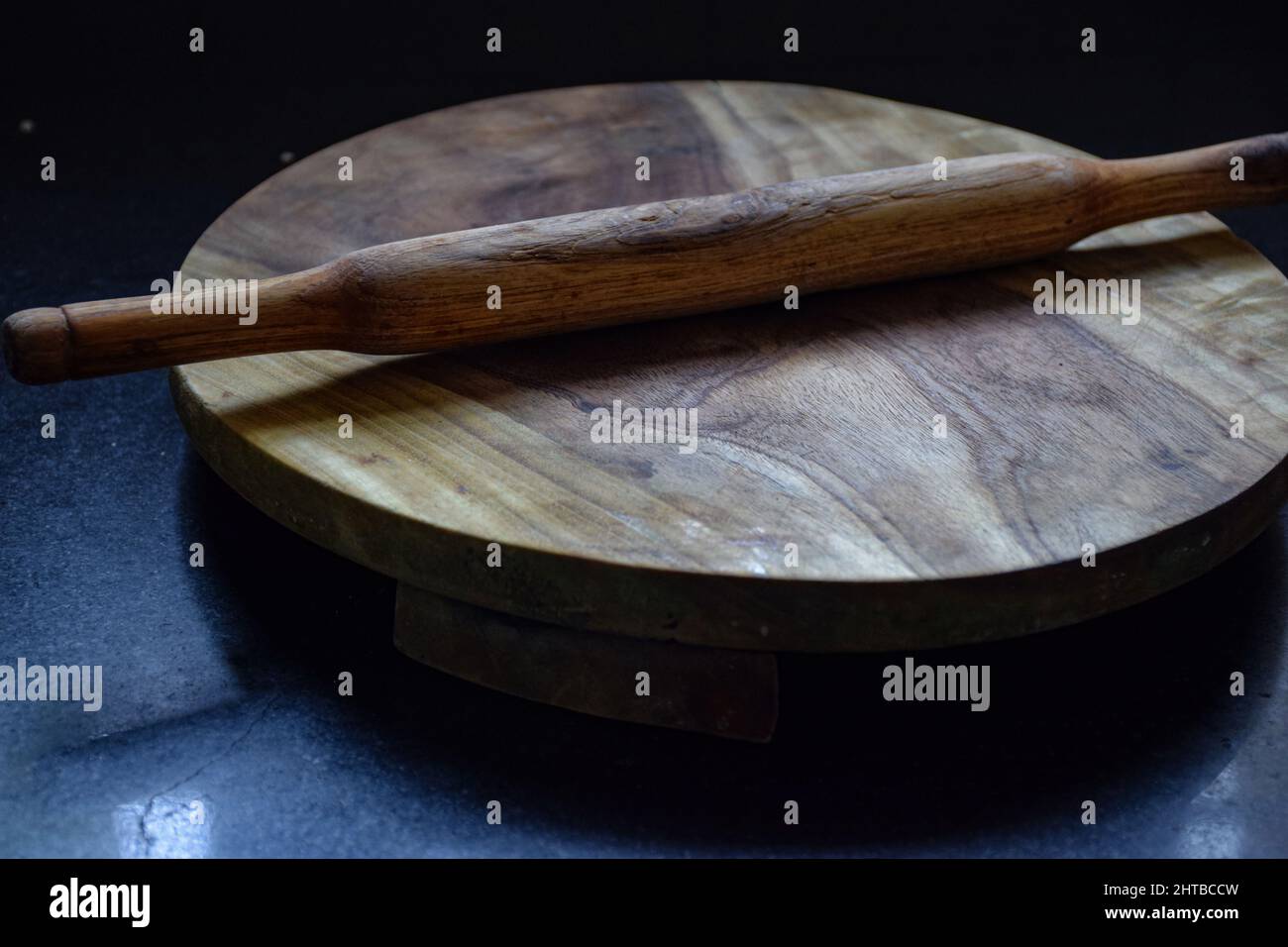 Closeup of a brown color wooden rolling pin on a black granite kitchen ...