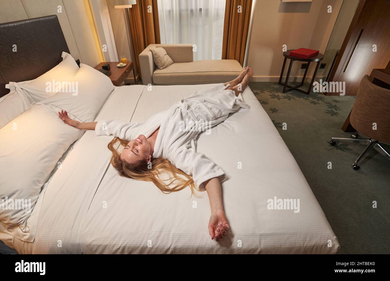 Relaxed woman spreading arms while lying on bed Stock Photo - Alamy