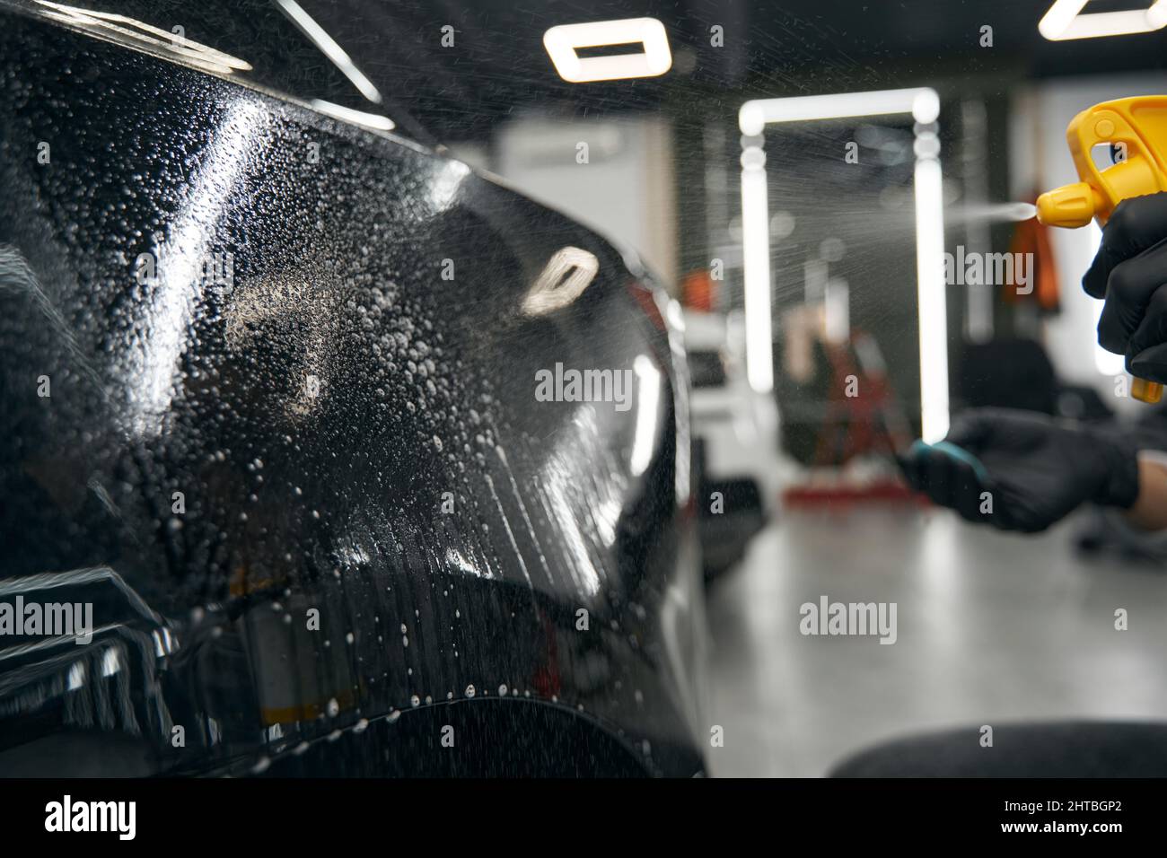 Gloved hands spraying exterior of motor vehicle with lubricating agent ...