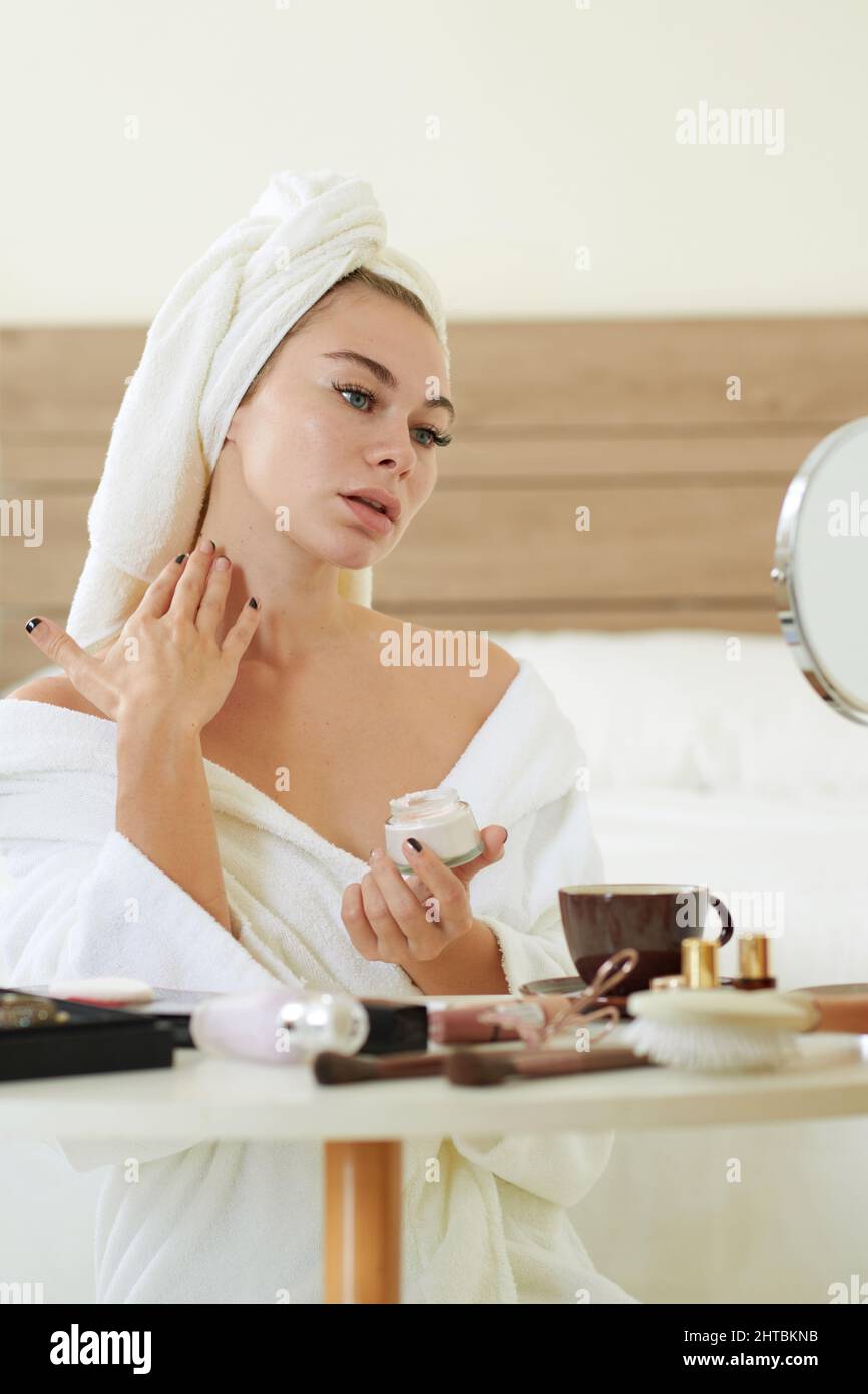 Young woman applying cream on neck and chest that helps to firm skin ...