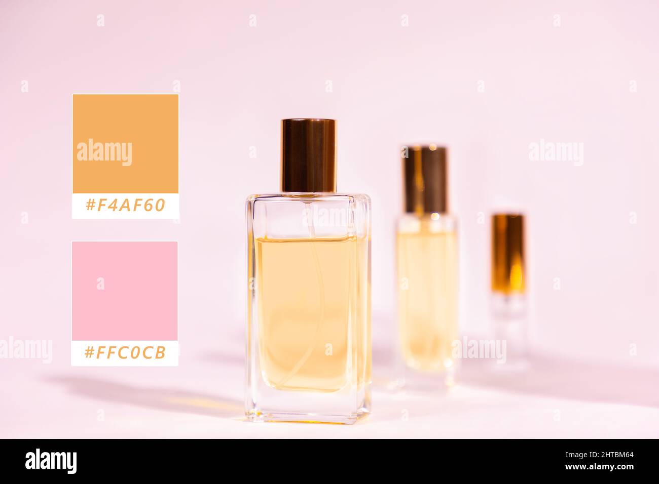 Three transparent glass perfume bottles on a pastel pink background ...