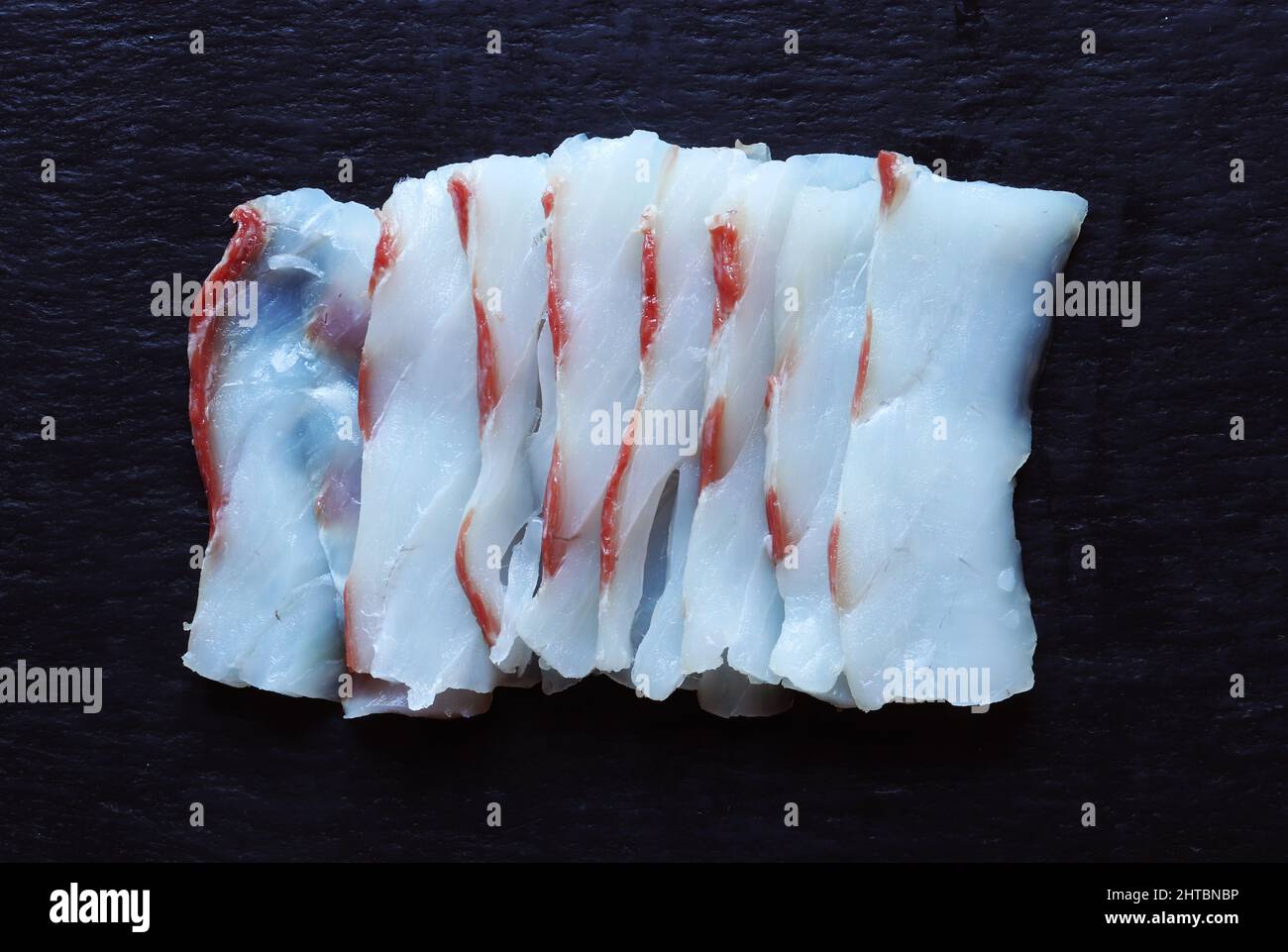 Top view of a filet of meager cut like sashimi on slate background ...