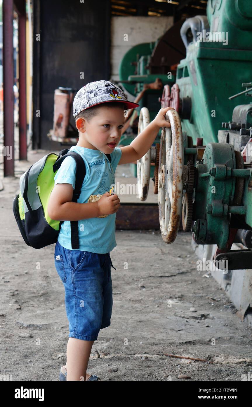 Young boy spinning a metal wheel of a locomotive at an outdoor museum ...