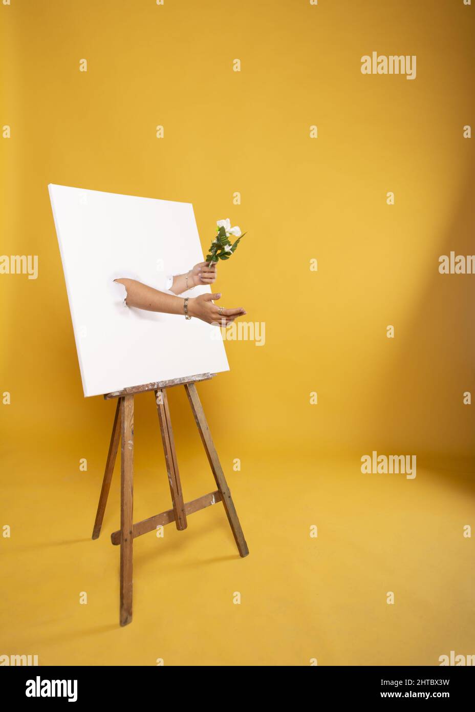 Vertical shot of an easel with canvas and hands holding a flower coming ...