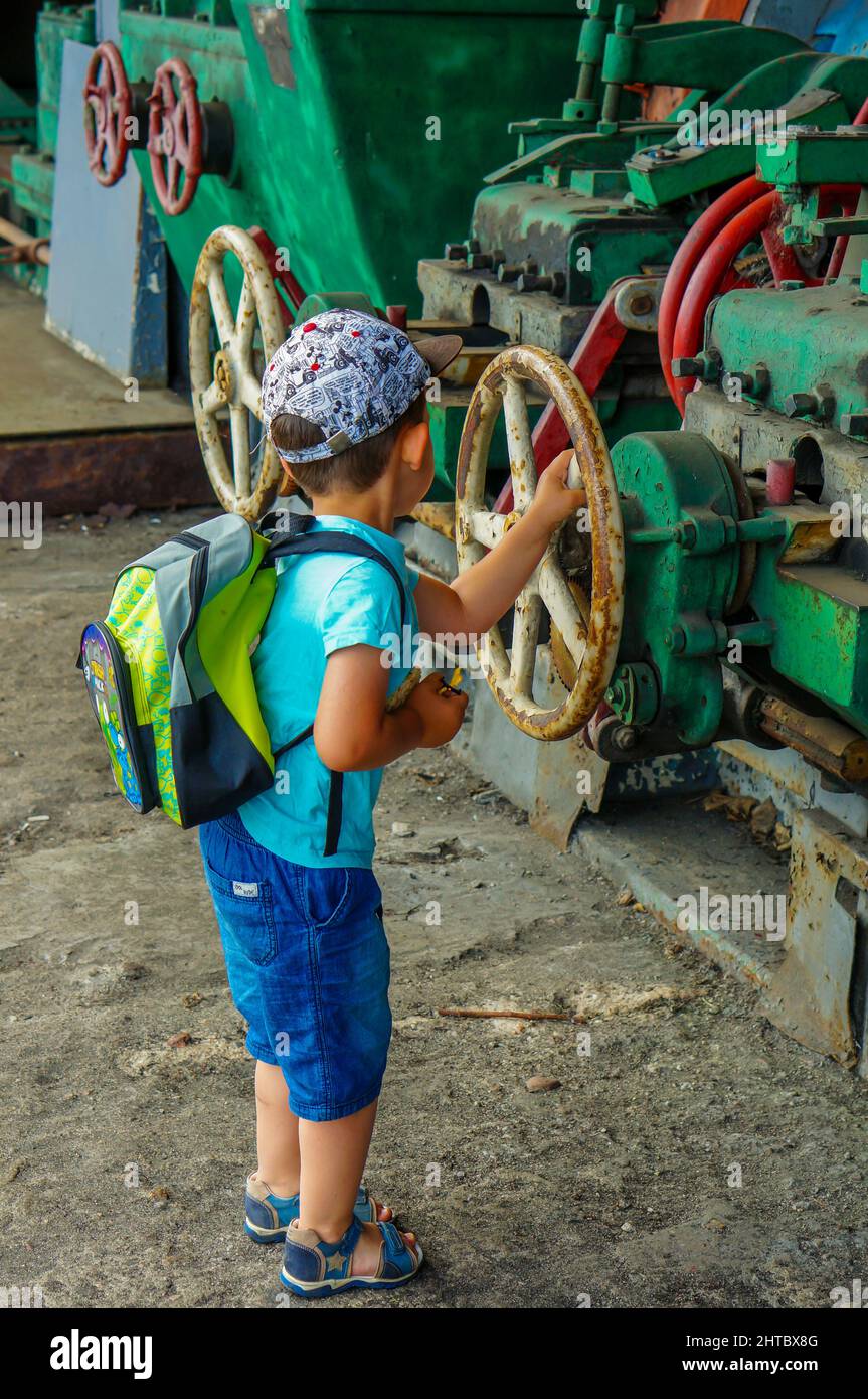 Young boy spinning a metal wheel of a locomotive at an outdoor museum ...