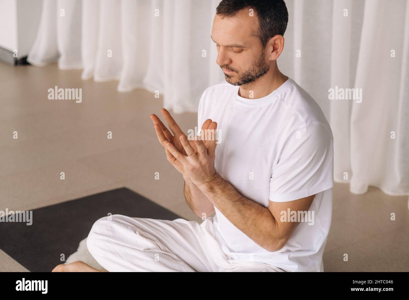 a man in white sportswear is doing yoga with a fitness room. the ...