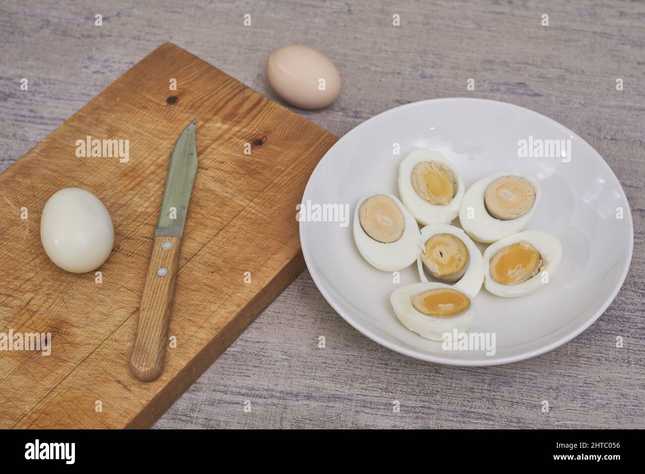 Boiled eggs cut in pieces on a white plate with a knife and wooden ...