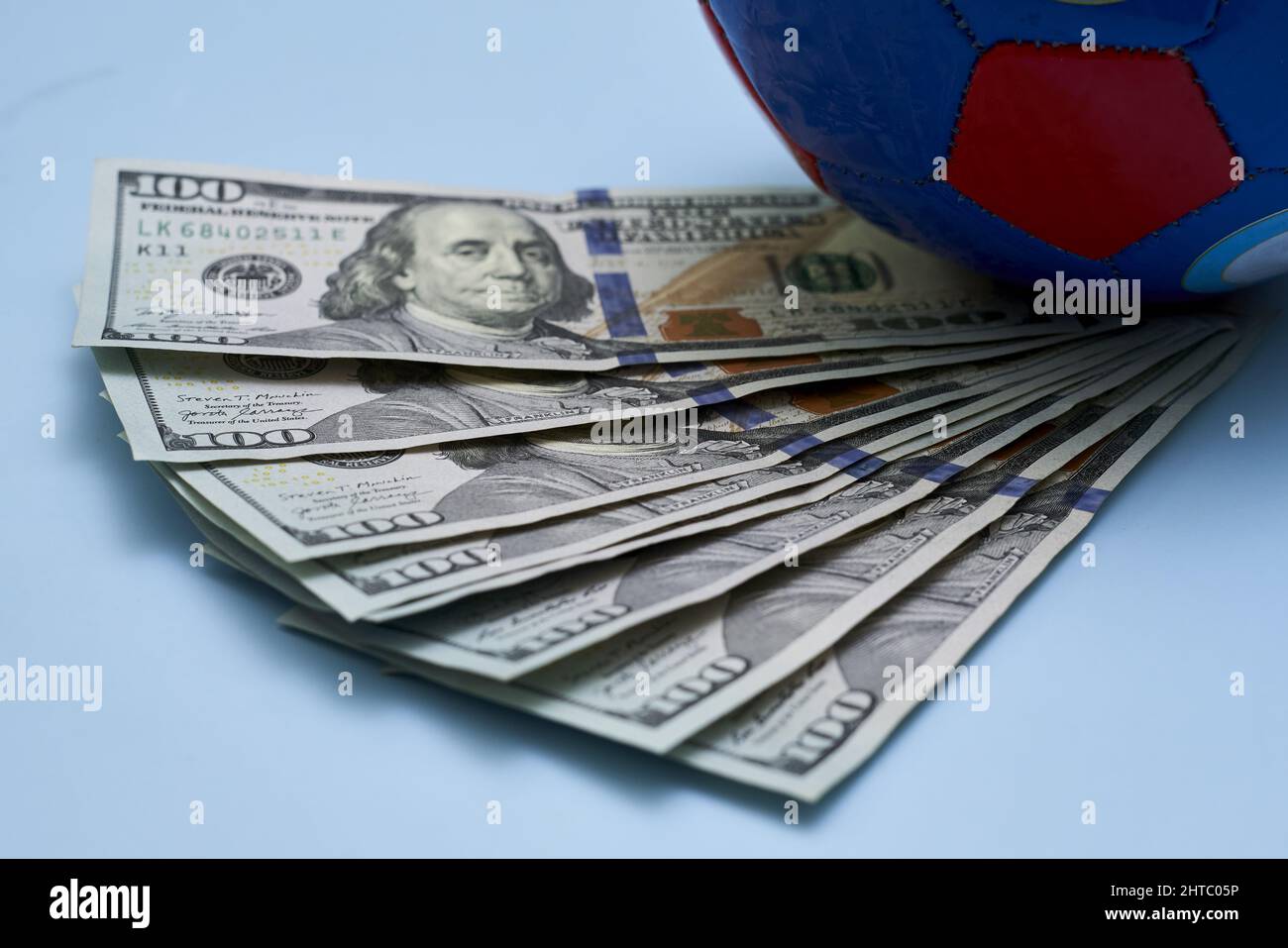Closeup shot of a pile of money under a football on a blue background ...