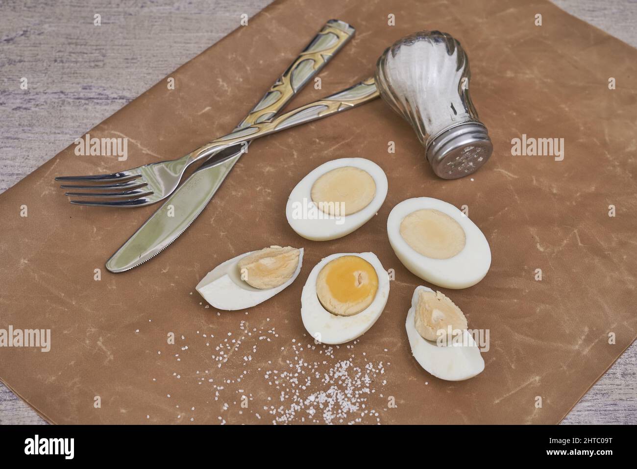 Boiled eggs cut in pieces on a wooden table with a fork and knife Stock ...
