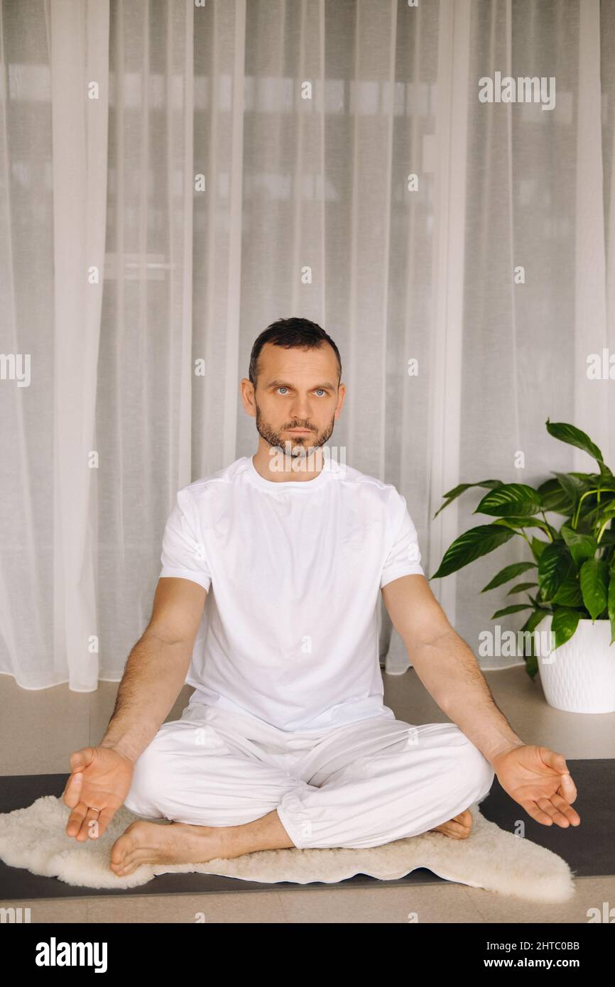 a man in white sportswear is doing yoga with a fitness room. the ...